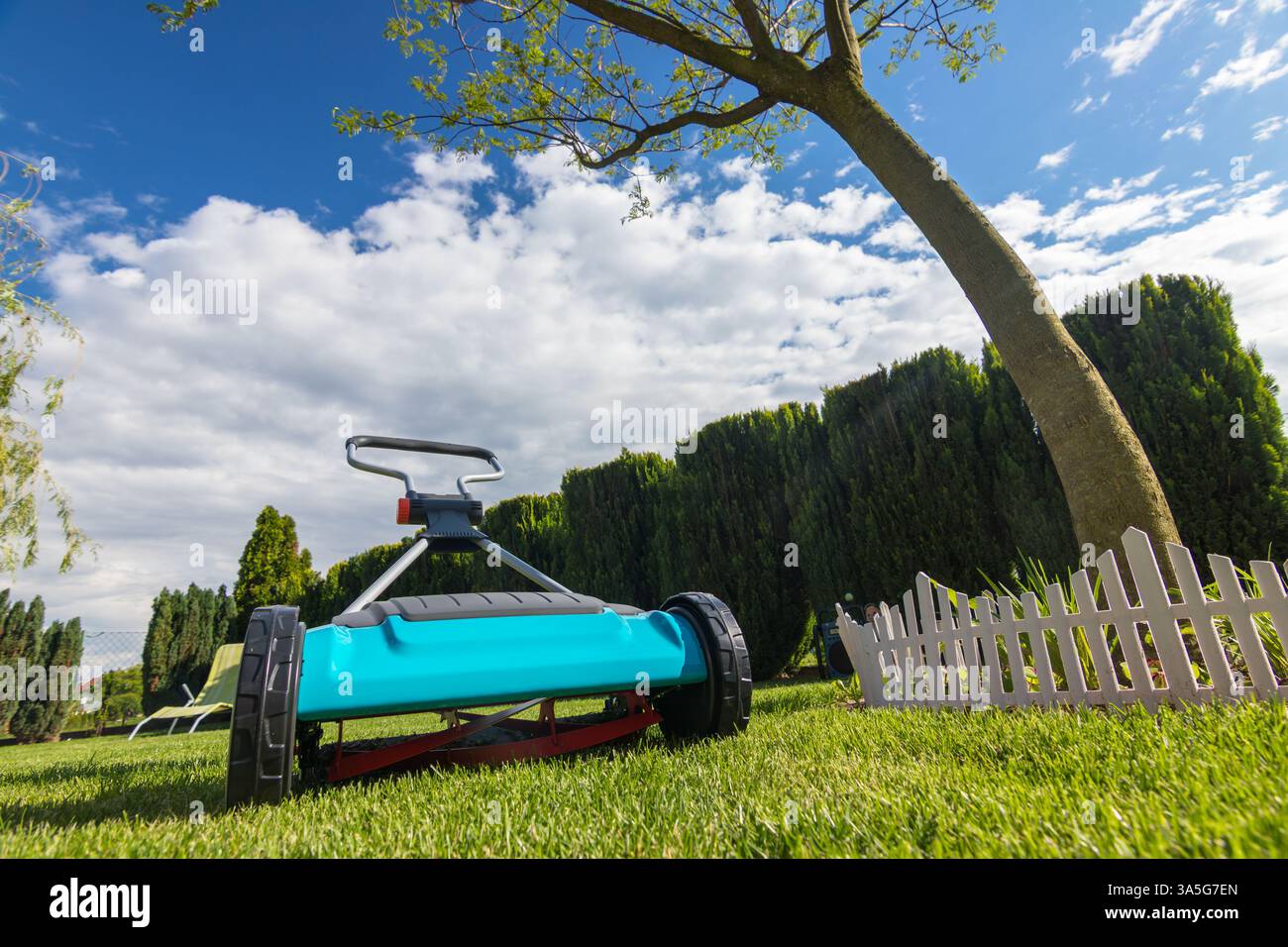 A vibrant backyard scene with a manual lawn mower on a green lawn under ...