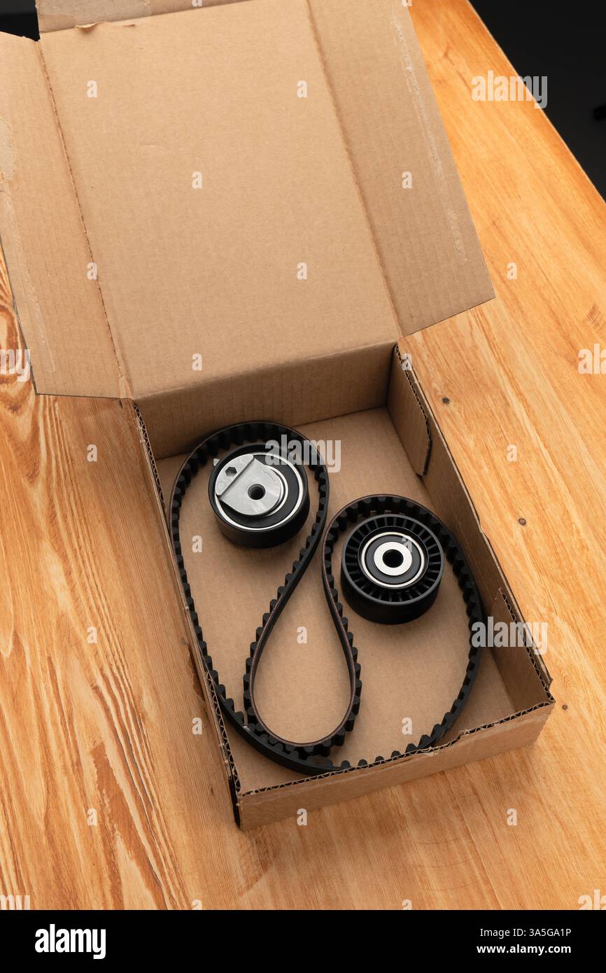 New timing belt kit with rollers in a cardboard box on a wooden table ...
