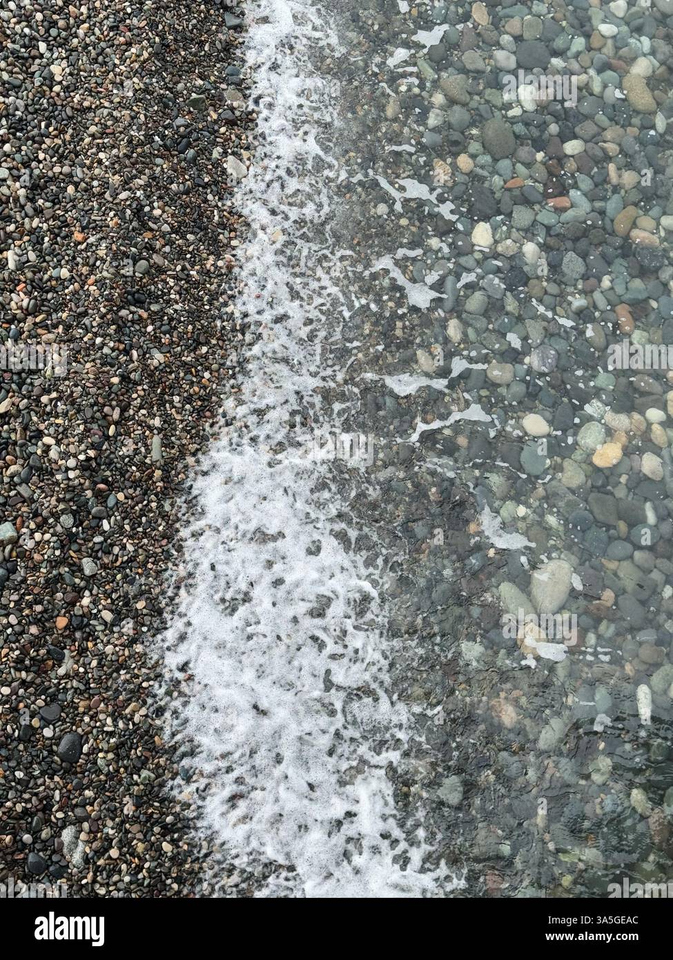 Aerial view of ocean waves washing over a pebble beach, showing the ...