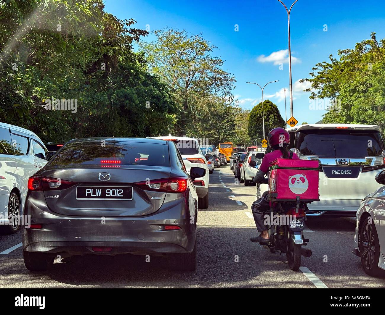 Delivery driver on motorbike weaving through traffic in Penang ...