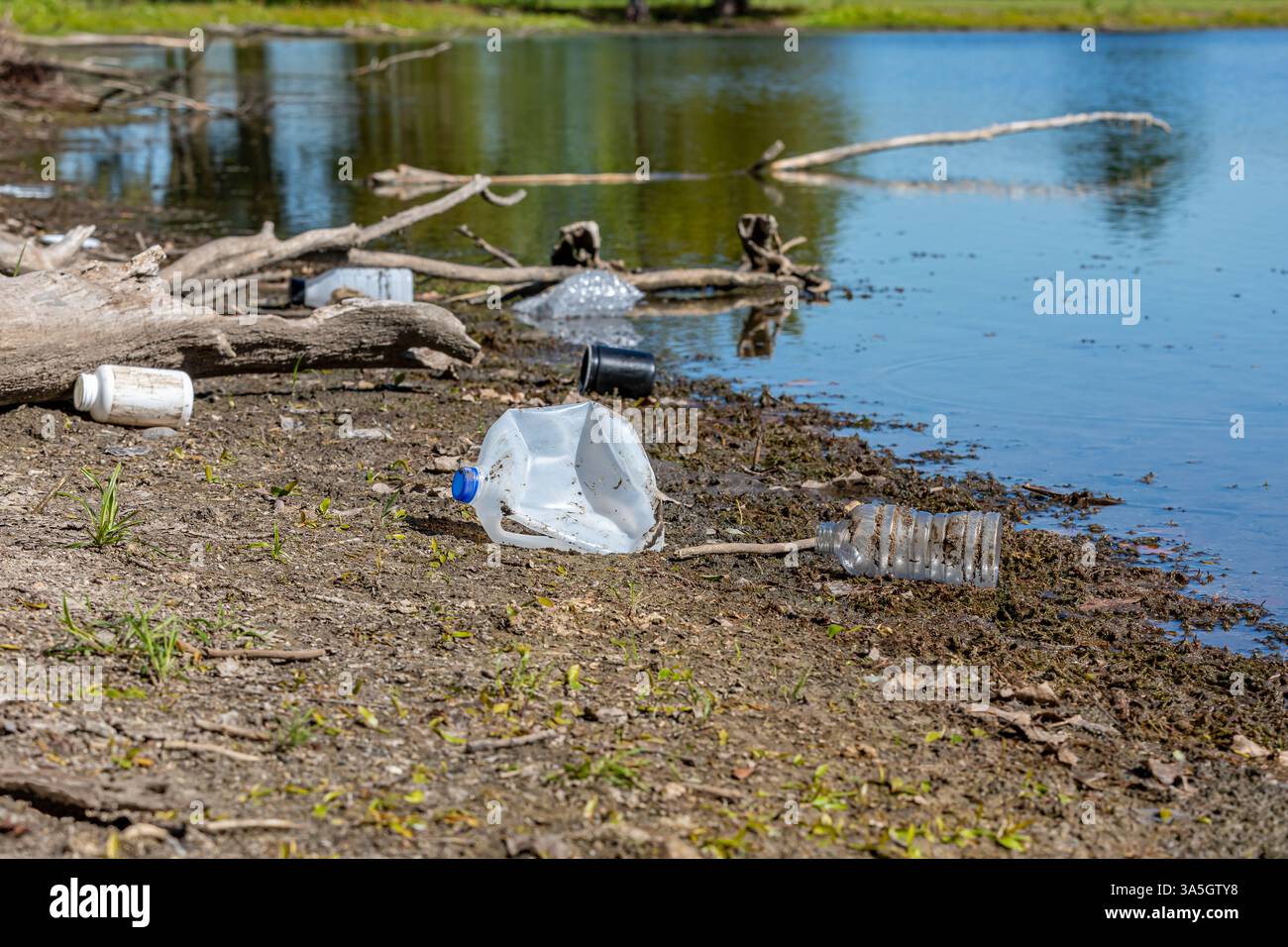 Plastic bottle and trash along shoreline. Waterway pollution, recycling ...