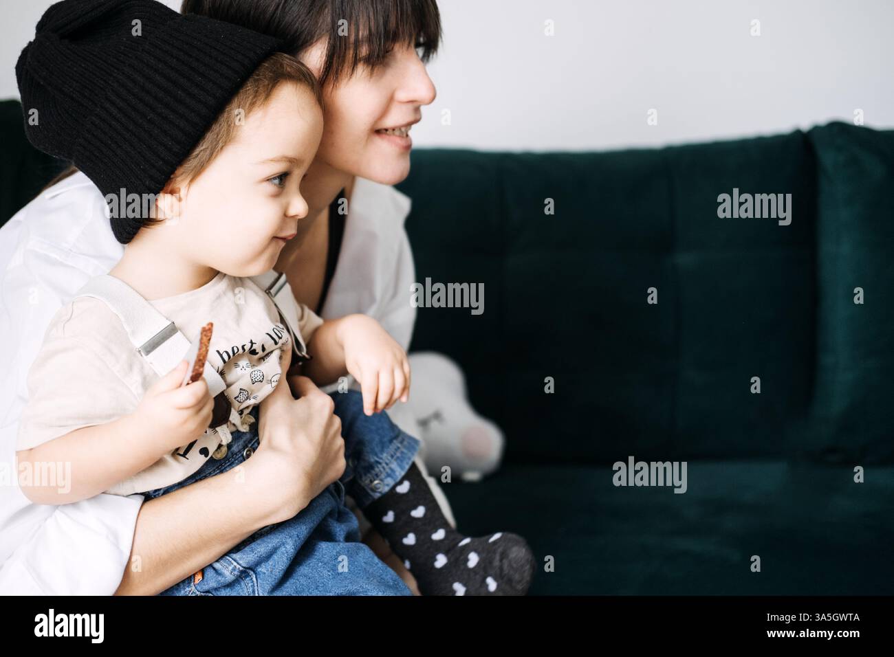 Mother and toddler wearing beanie sitting together on couch. Family ...