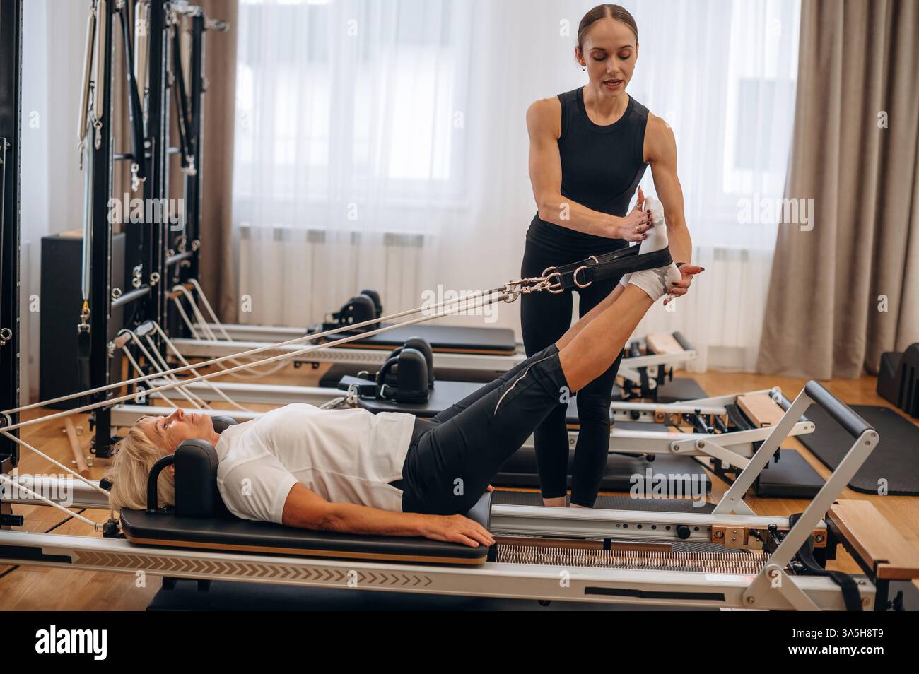 Laying down and doing legs exercise. Female trainer is helping old ...