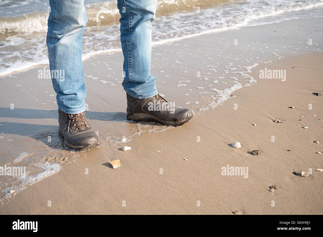 legs of a man in blue jeans, standing on the shore in hiking boots ...