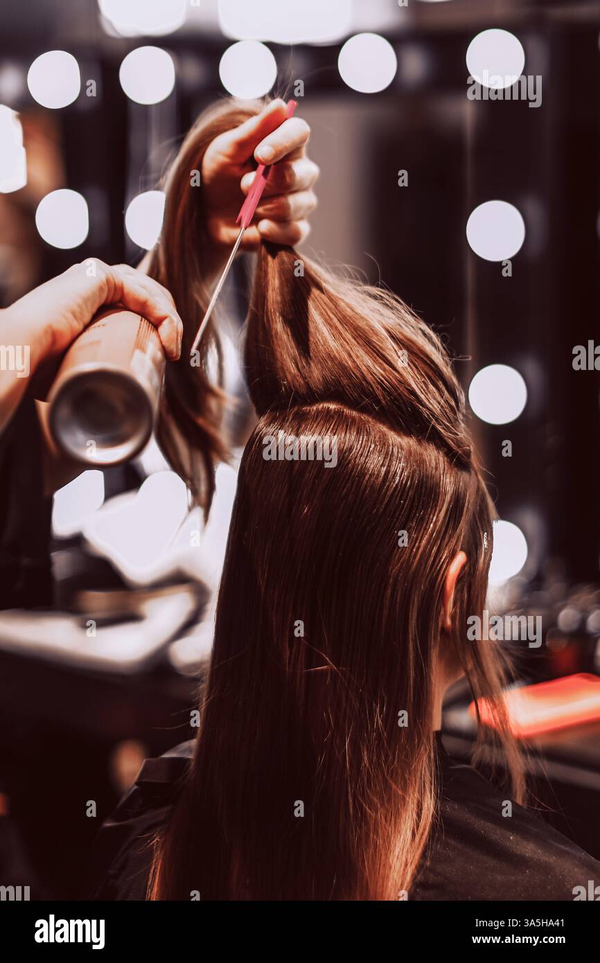 Female hands of a stylist doing a hairstyle of a young fashion model ...