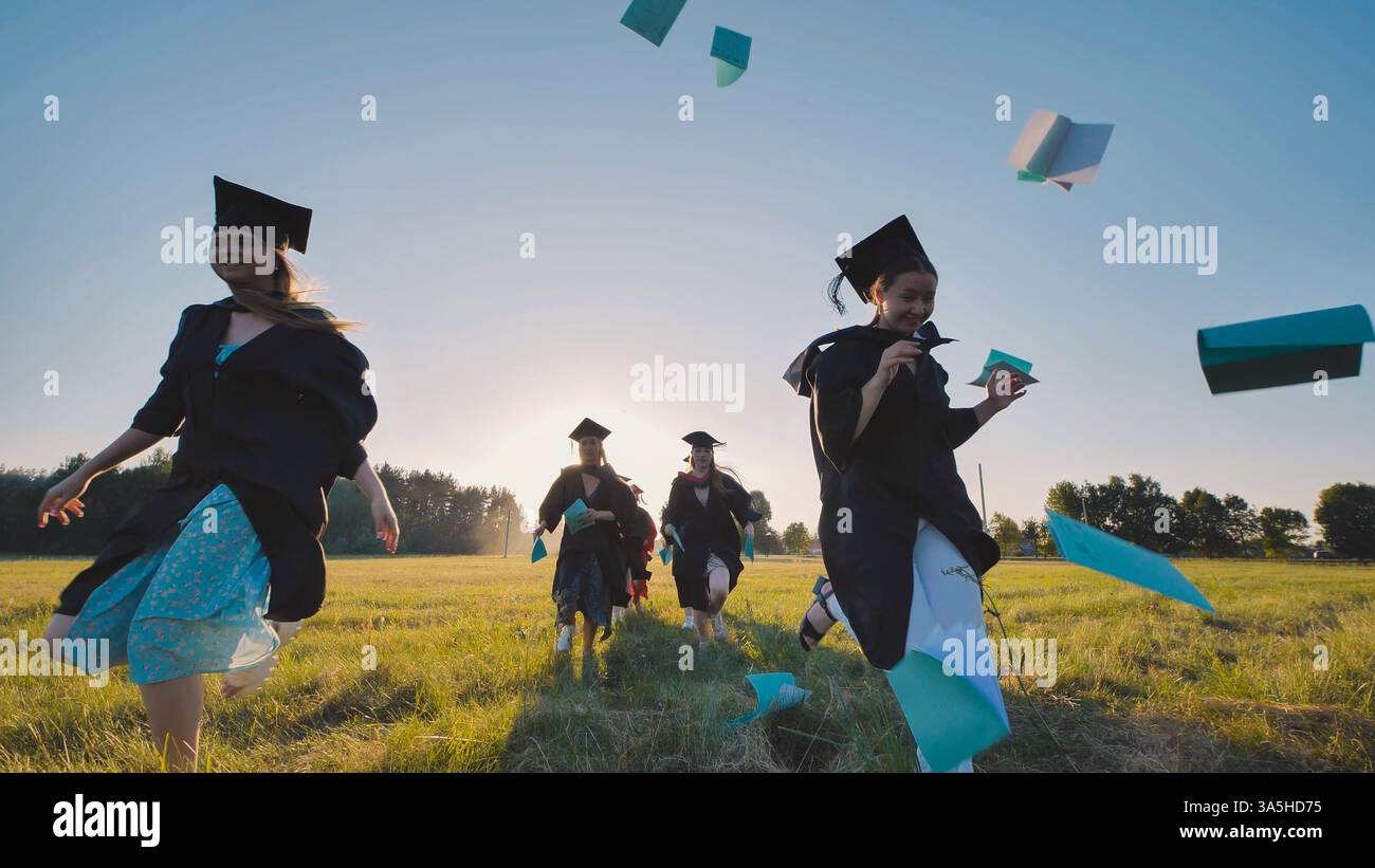 Graduates throwing notebooks in the air, running on a meadow ...
