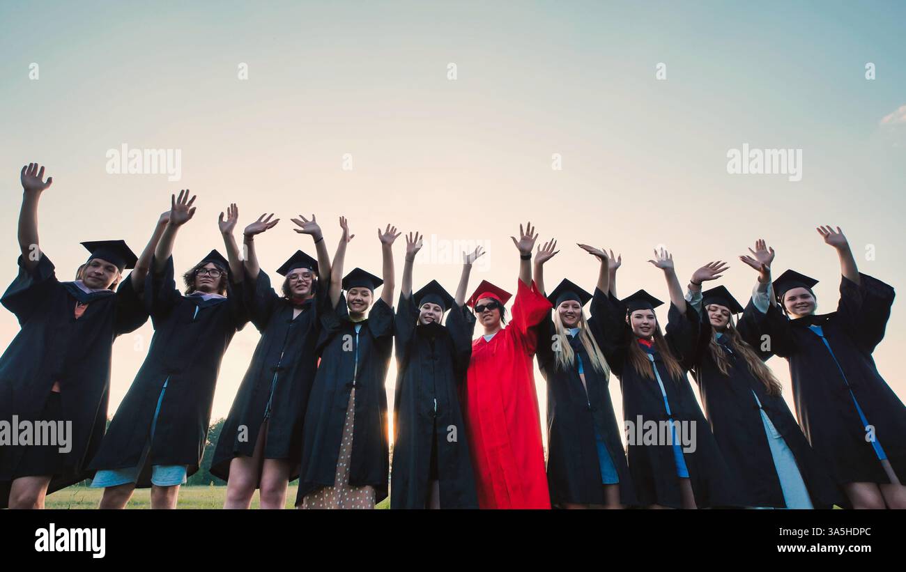 Group of joyful graduates in academic gowns and caps raising hands ...