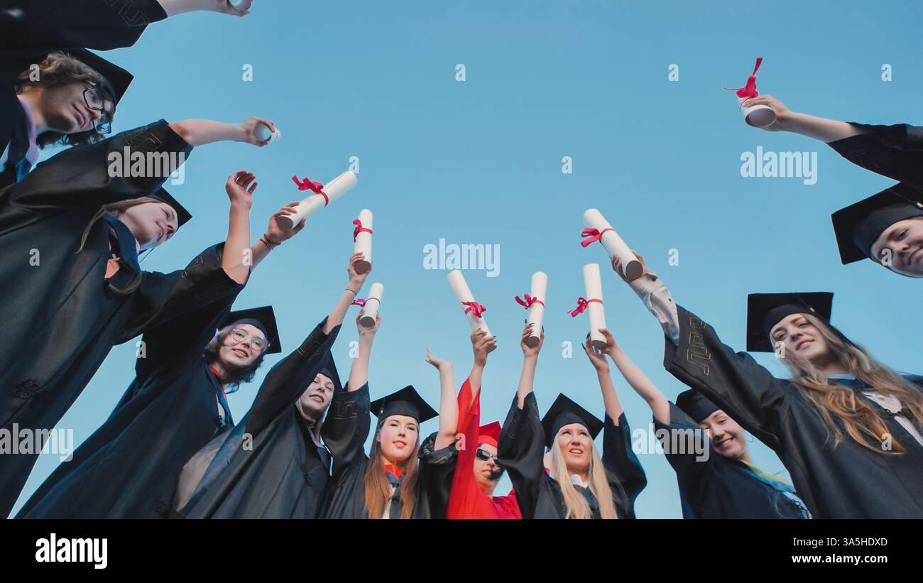 Cheerful graduates celebrating their academic achievement by raising ...