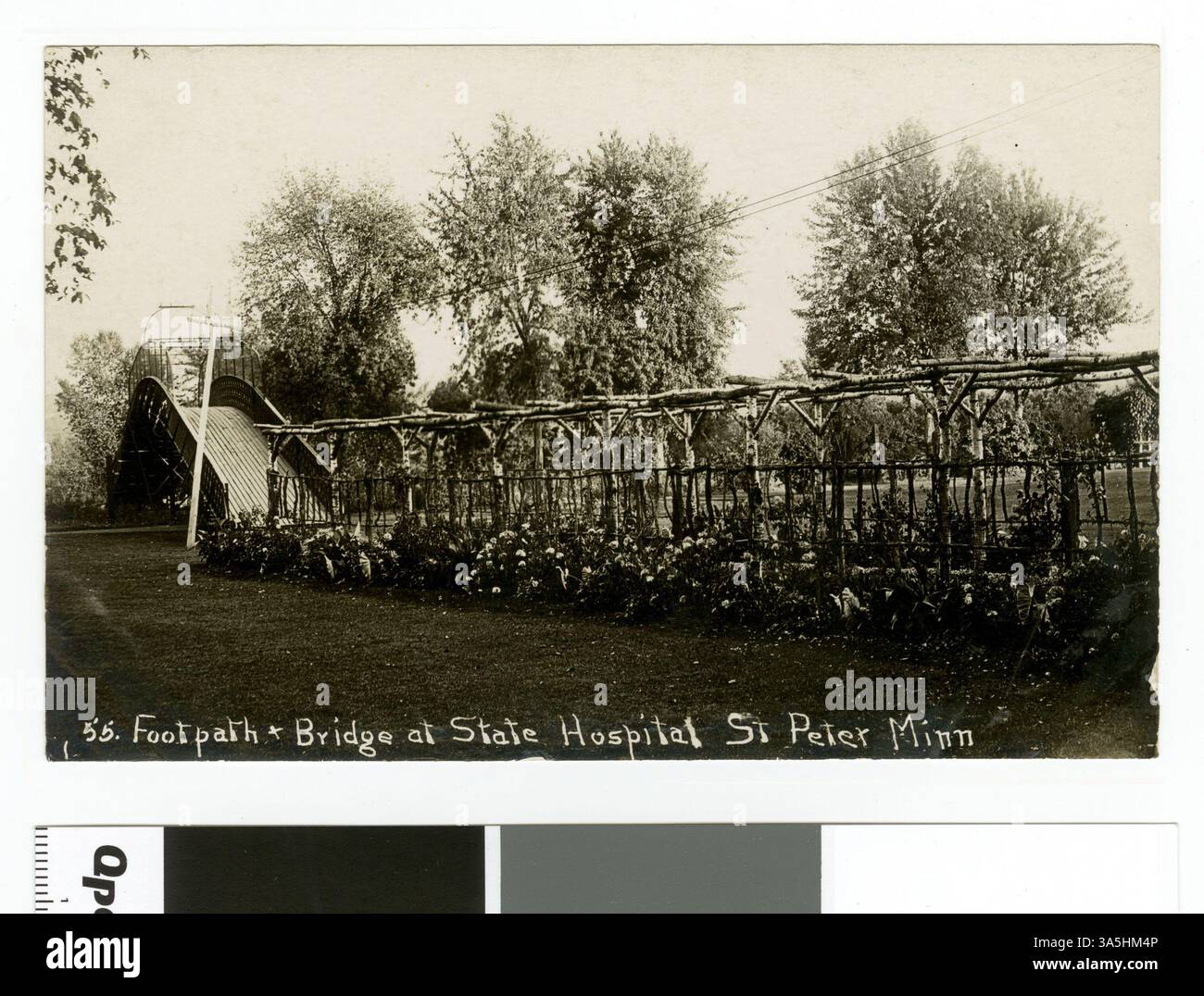 This postcard depicts a footpath and bridge over railroad tracks on the ...
