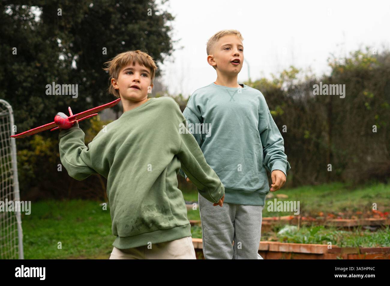 Two kids playing with a red toy airplane in a backyard garden, enjoying ...