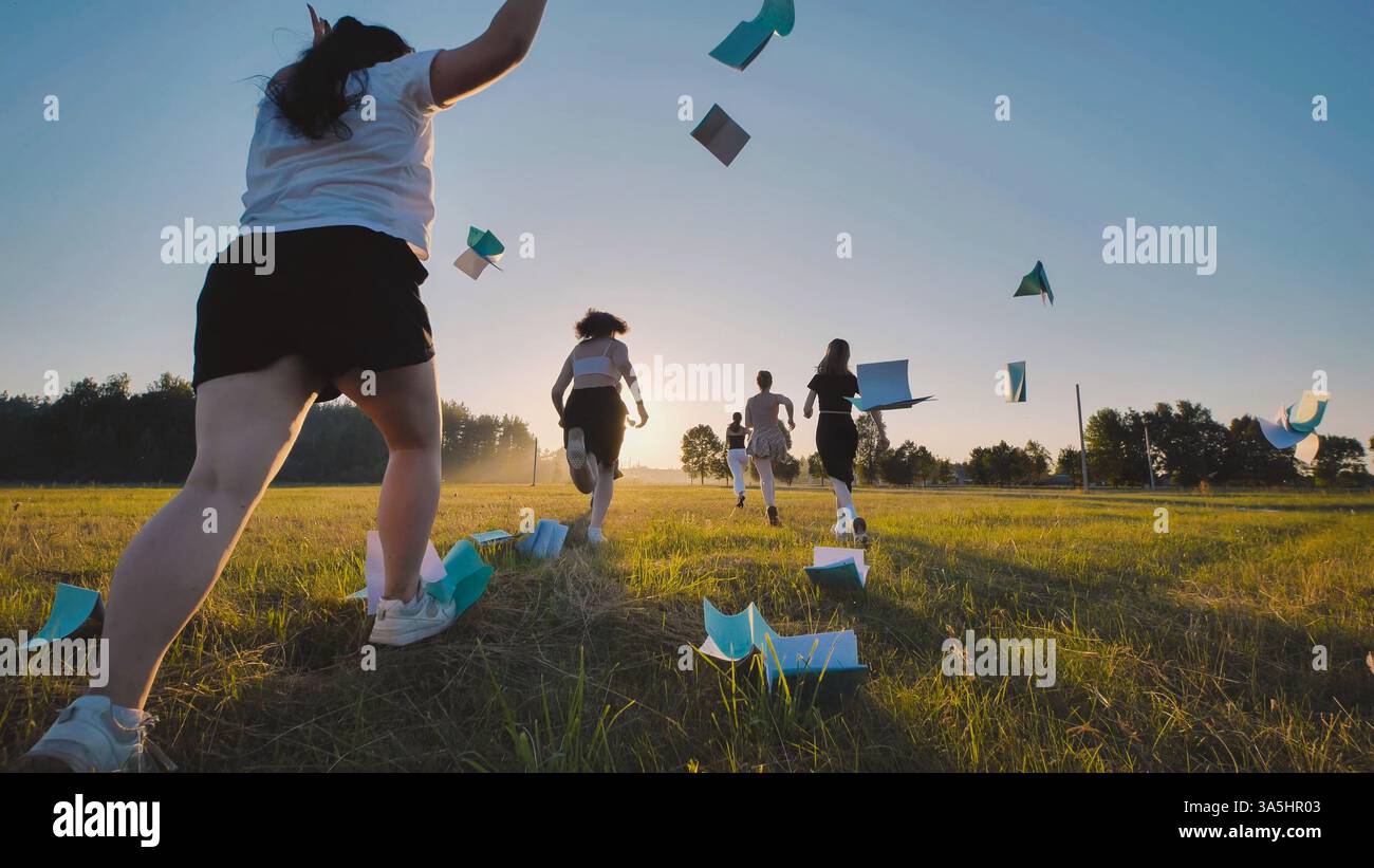 Teenagers are running in a field and throwing notebooks in the air ...