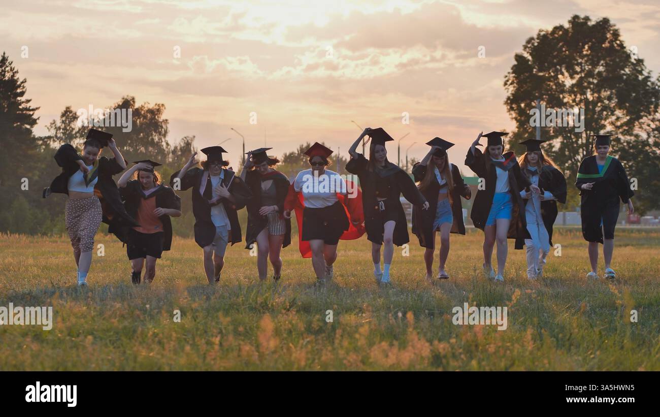 Group of cheerful graduates running together in a field, celebrating ...