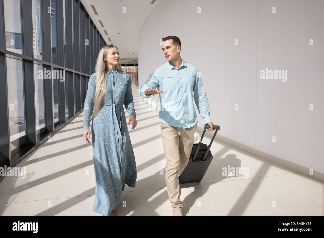 Young couple rolling suitcase moving toward gate. Two Caucasian male ...
