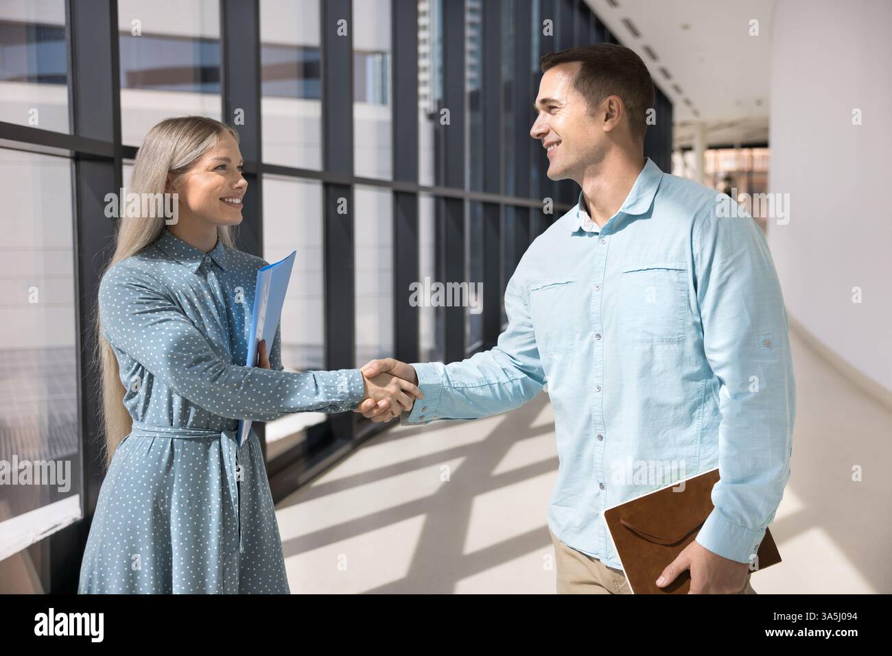 Two smiling European male, female colleagues talking, greeting each ...