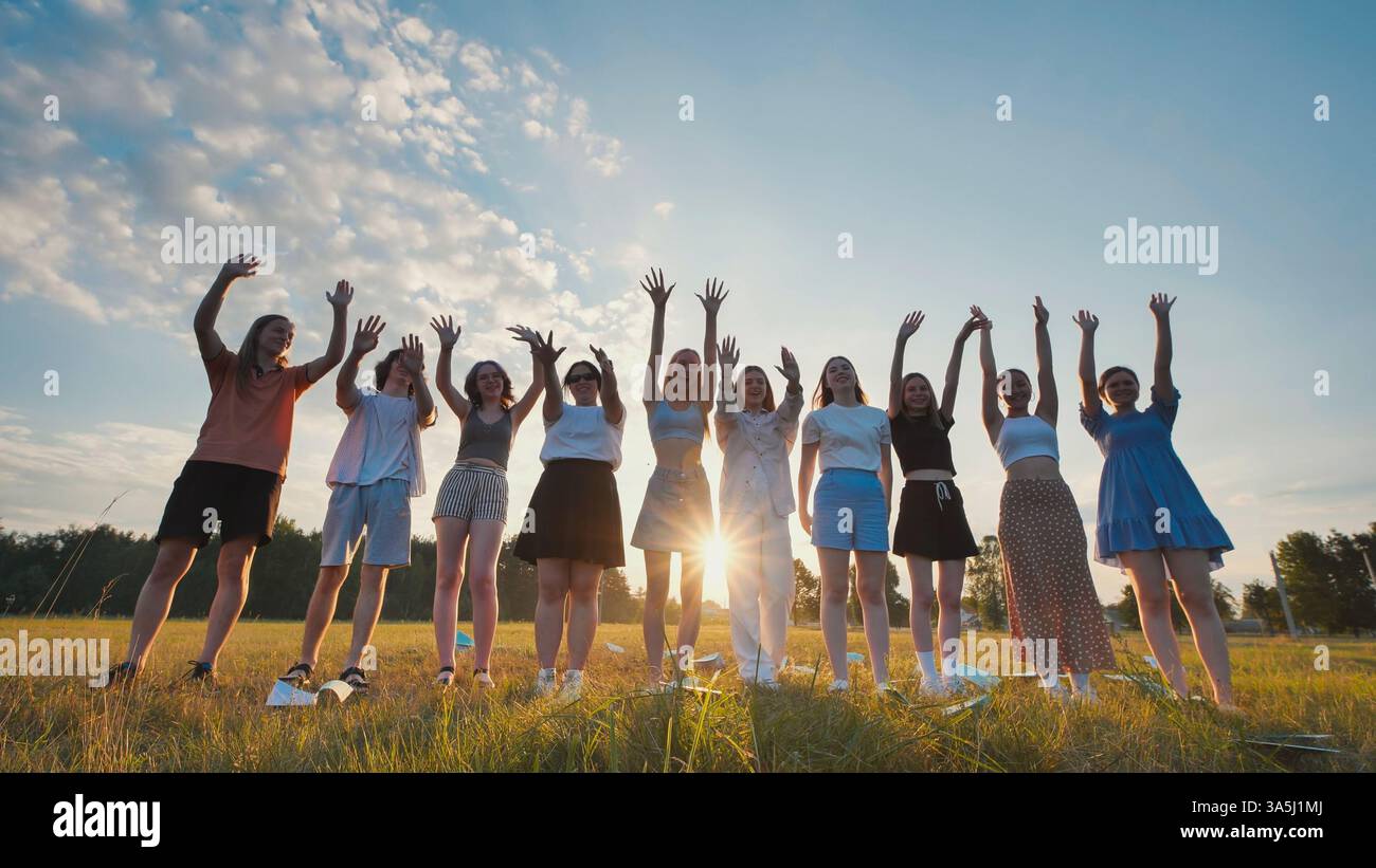 Group of happy students waving goodbye at sunset in a field ...