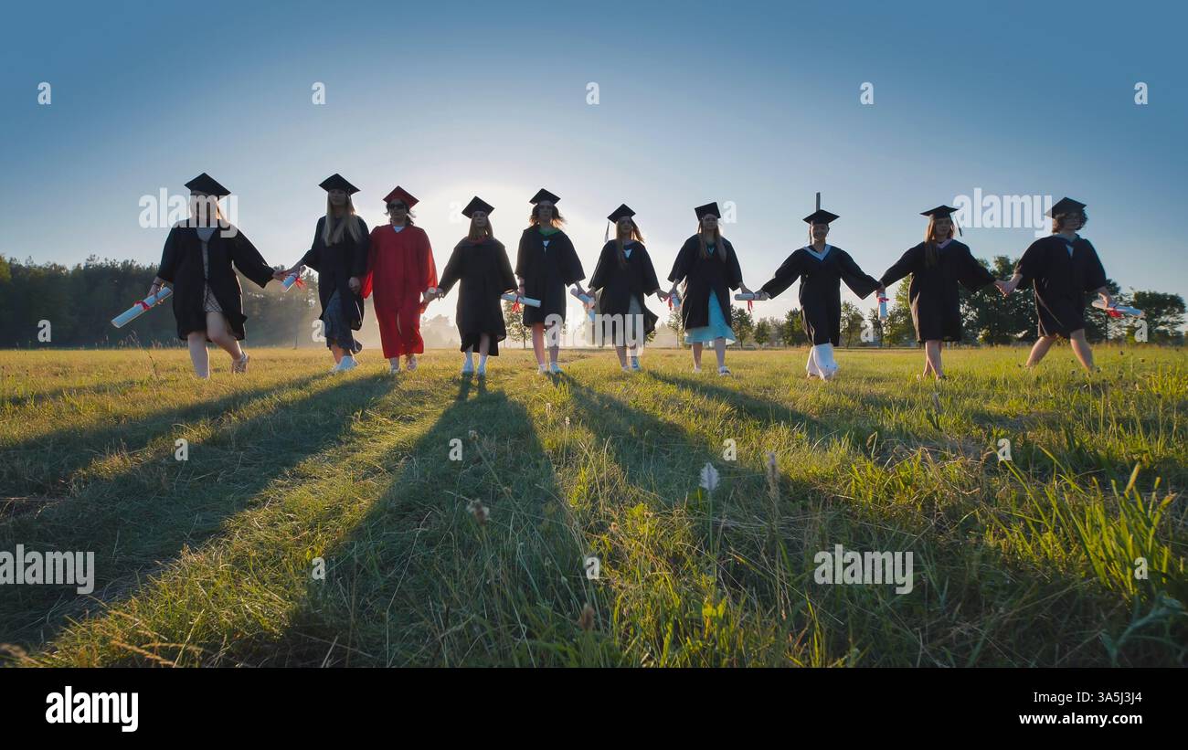 Group of cheerful graduates walking together in a field at sunset ...