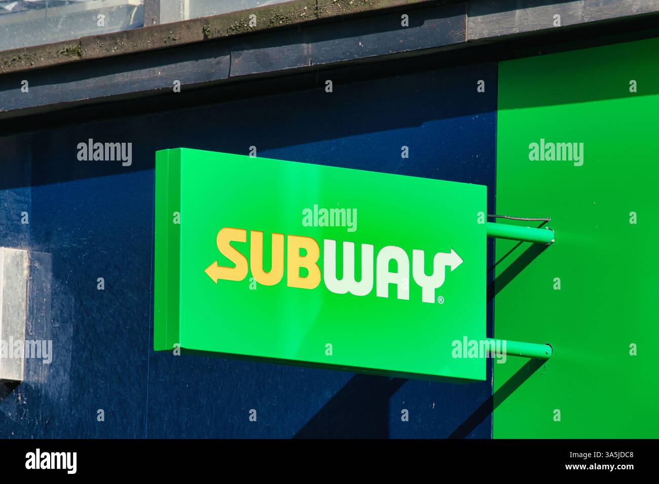 A brightly lit Subway sign is mounted on a dark blue and green building ...