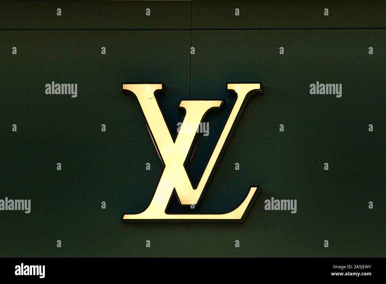 A golden "LV" logo is mounted on a dark green, textured surface. The ...