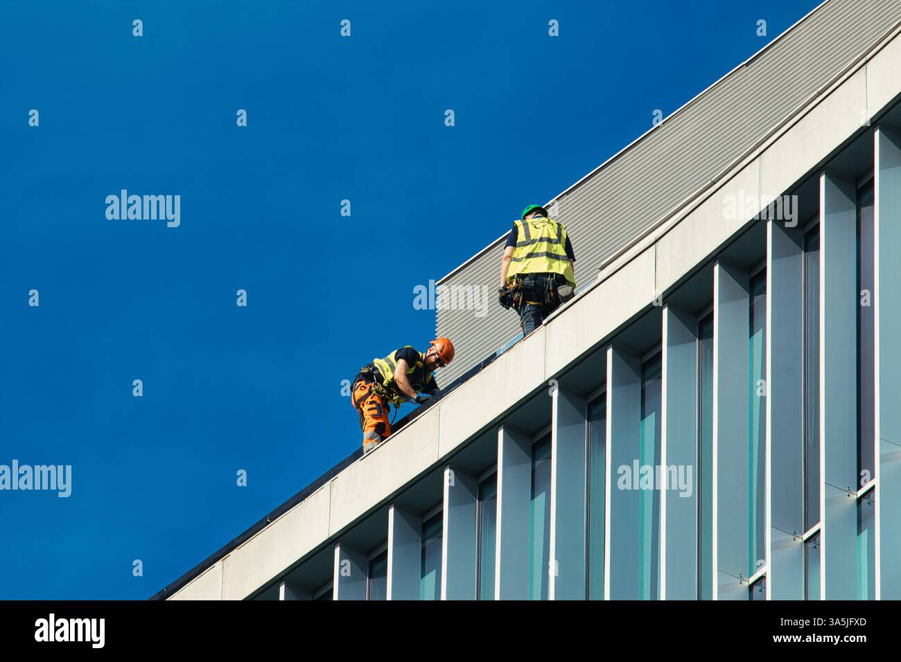 Two construction workers on the roof of a modern building against a ...