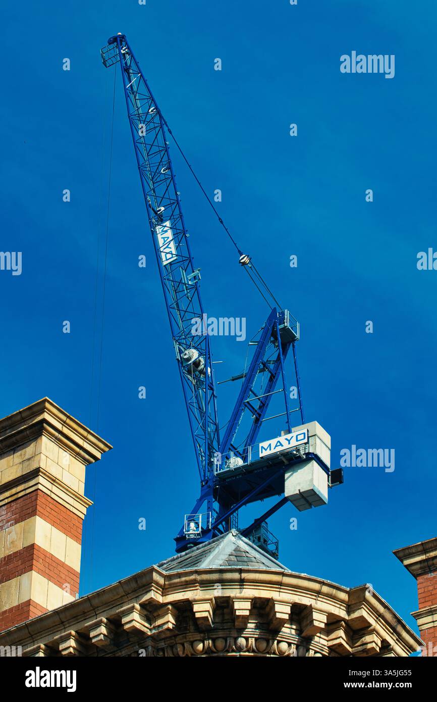 A blue construction crane rises above a building against a clear blue ...