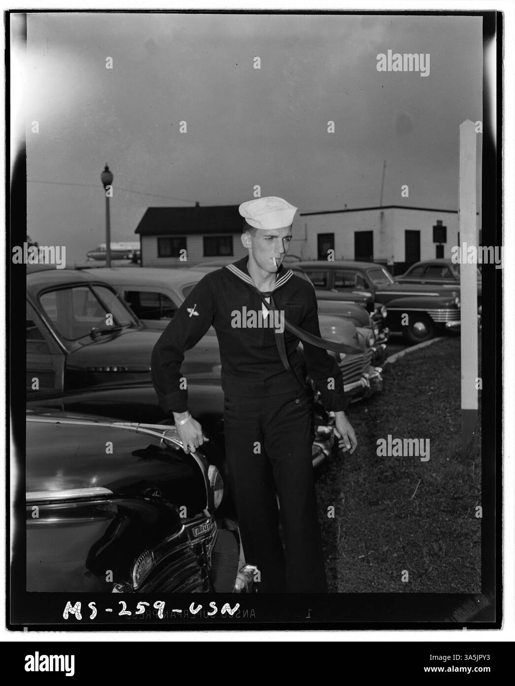 A sailor is seen smoking near a group of parked cars, captured in a ...