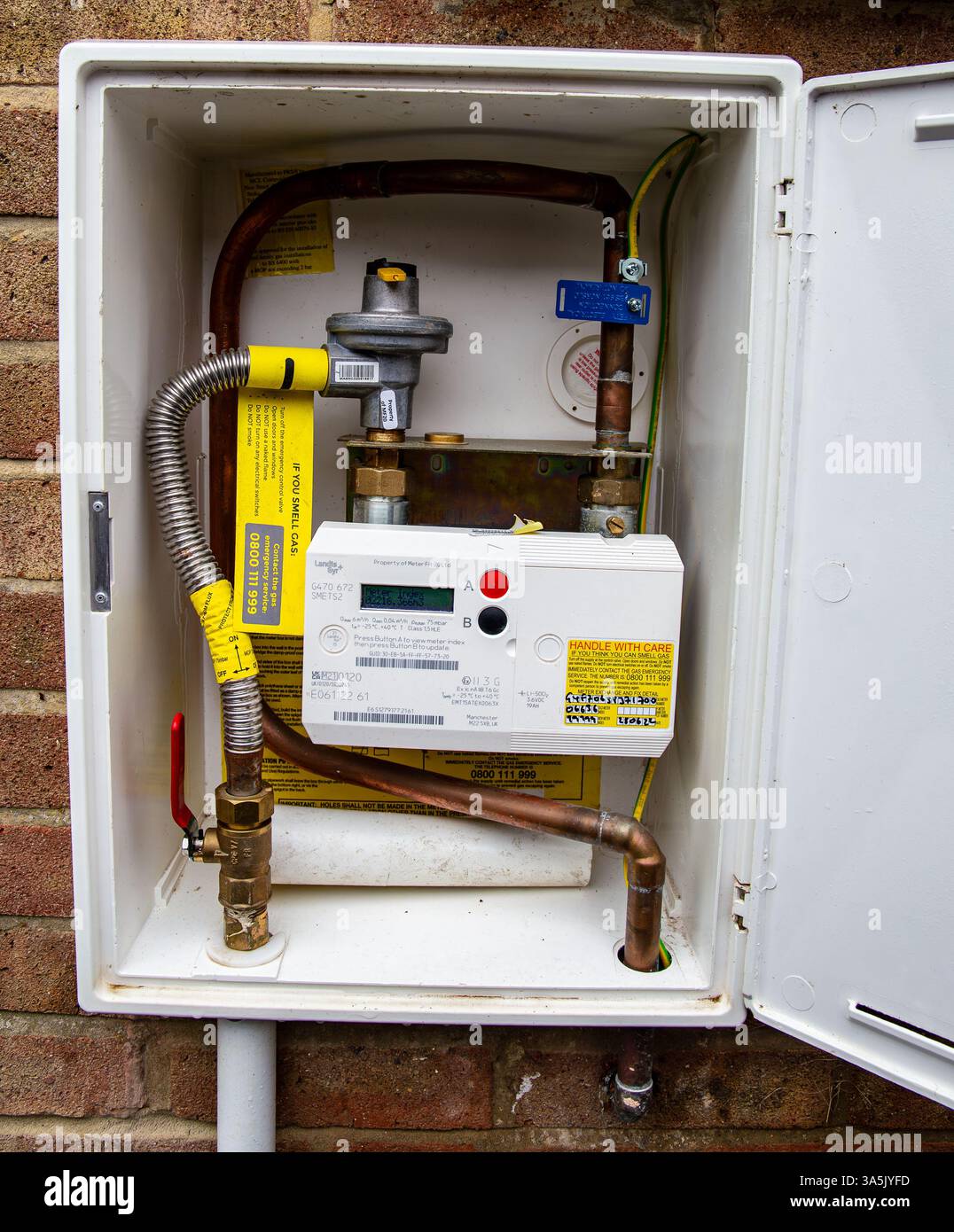 Outdoor gas meter box with pipes and wiring attached to a brick wall ...