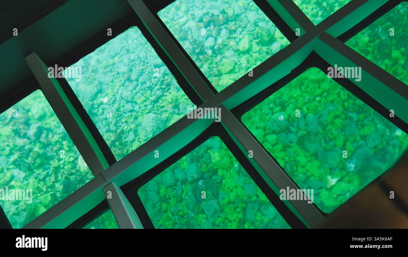 Square glass panels on the bottom of a boat reveal emerald green water ...