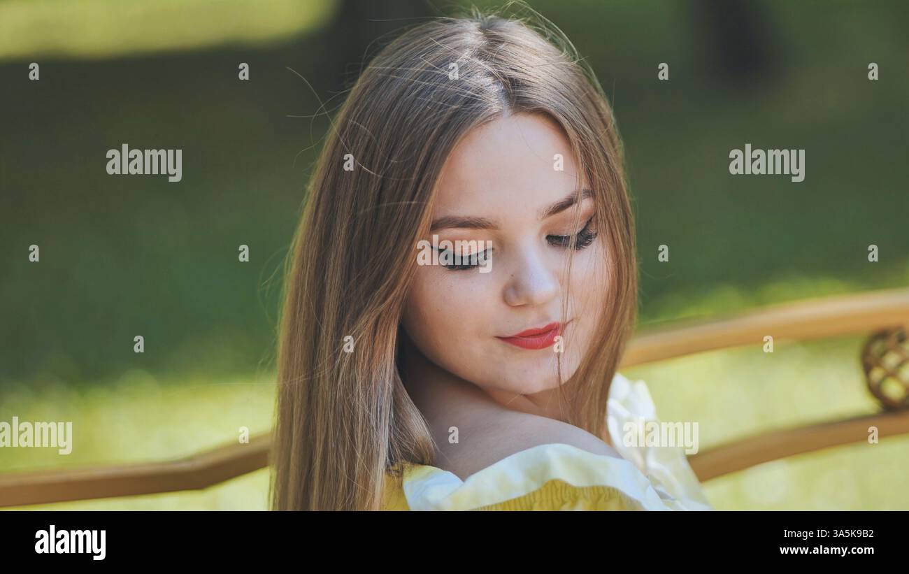Young woman with brown hair in yellow dress, sitting pensively on park ...