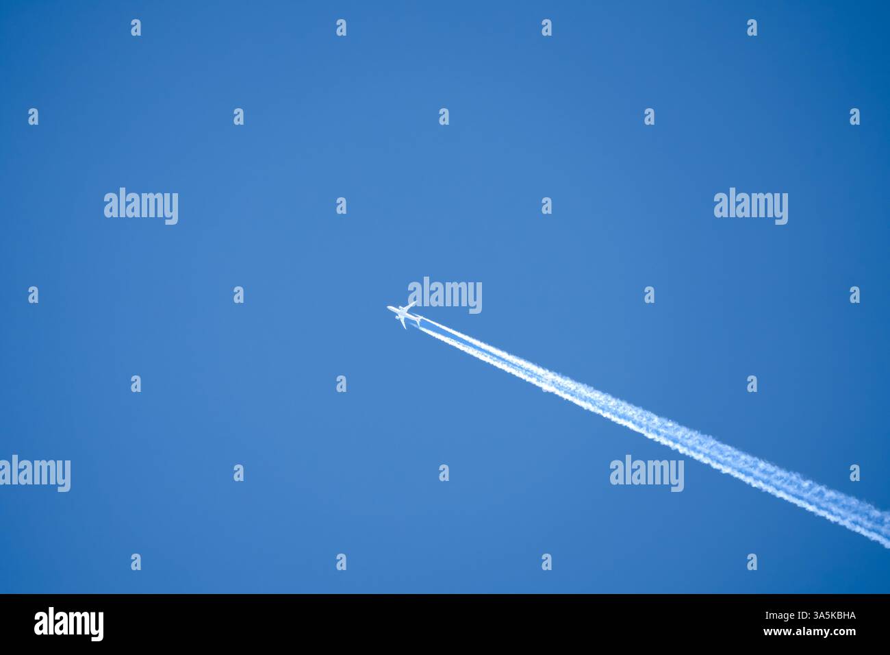 a twin engined jet liner aircraft in deep blue sky, contrails vapour ...