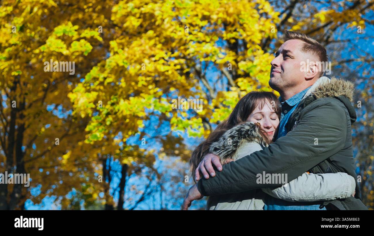 Loving couple embracing beneath golden hued trees, sharing intimate moment amid autumn sunlight ...