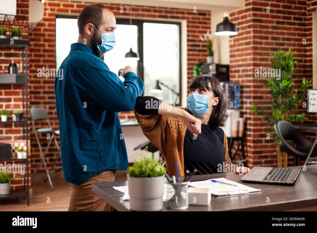 In bright office, businessman and woman exchange elbow bumps as part of ...