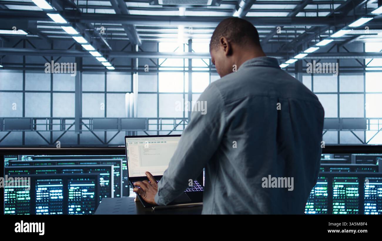 Computer scientist in server room coding on laptop, developing disaster recovery plans. African ...