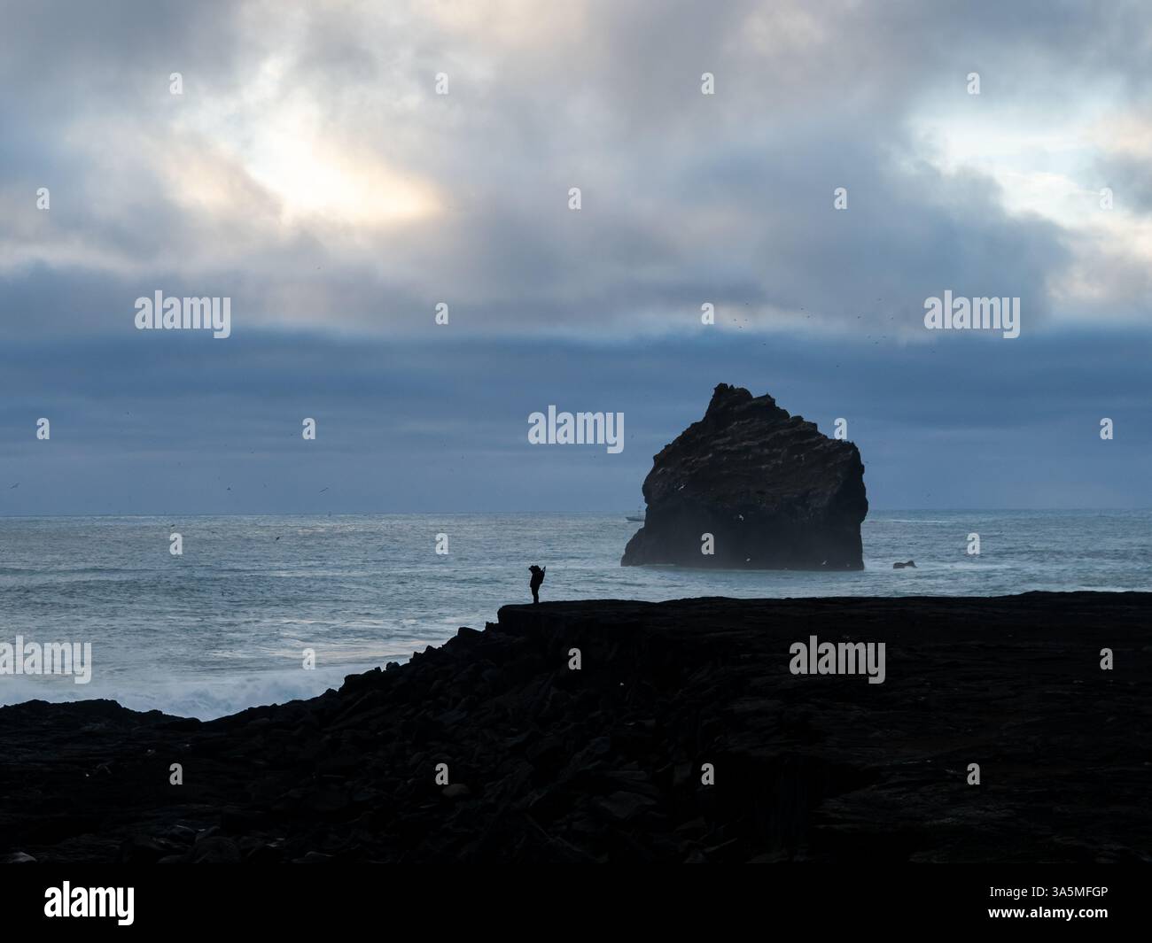 Lone traveler standing on the cliffs of Valahnúkamöl, gazing at a sea ...