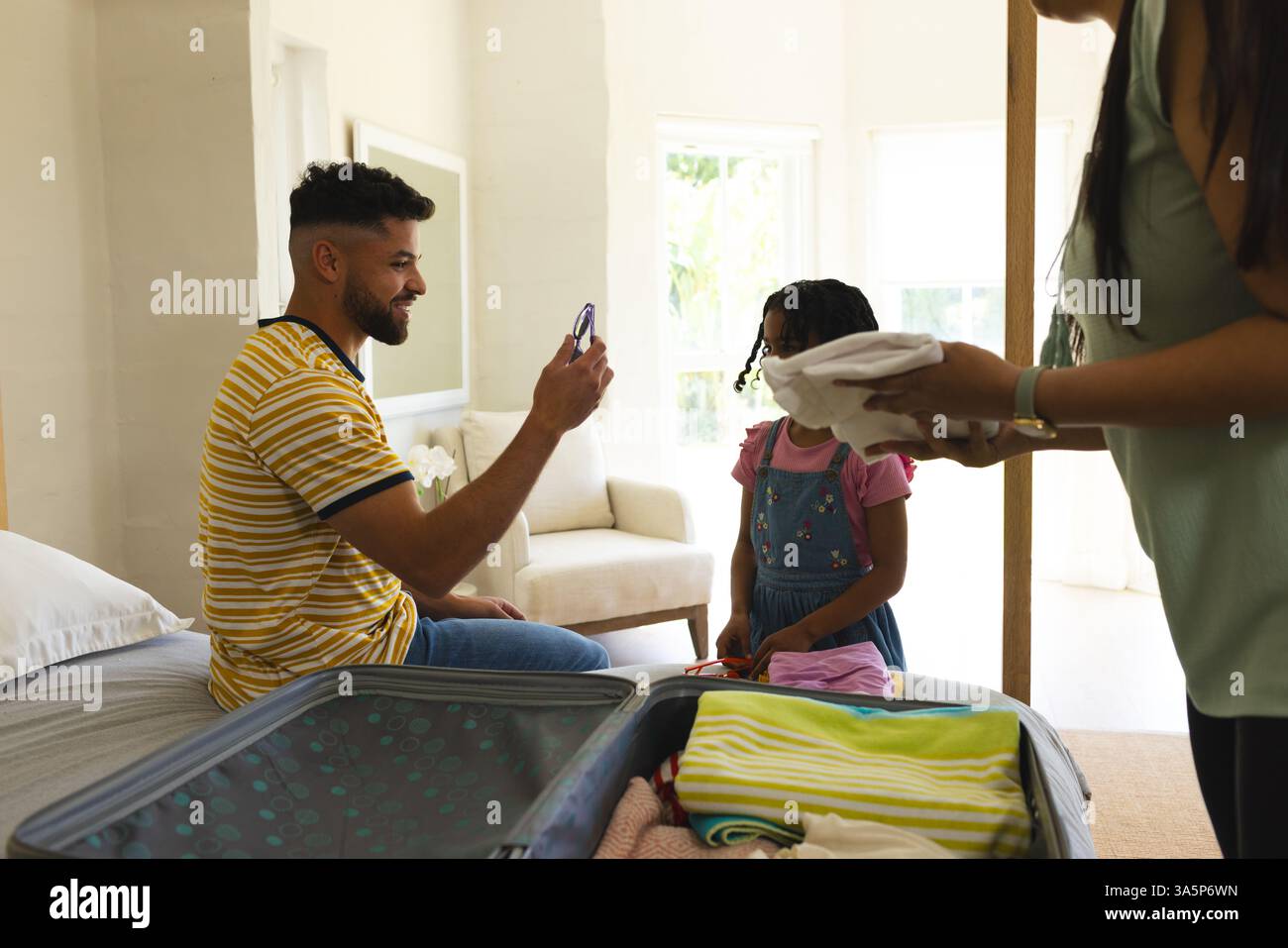 Father showing smartphone to daughter while mother packs suitcase in ...