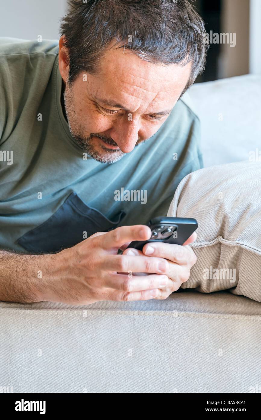 Lazy couch potato guy using mobile phone while laying on living room ...