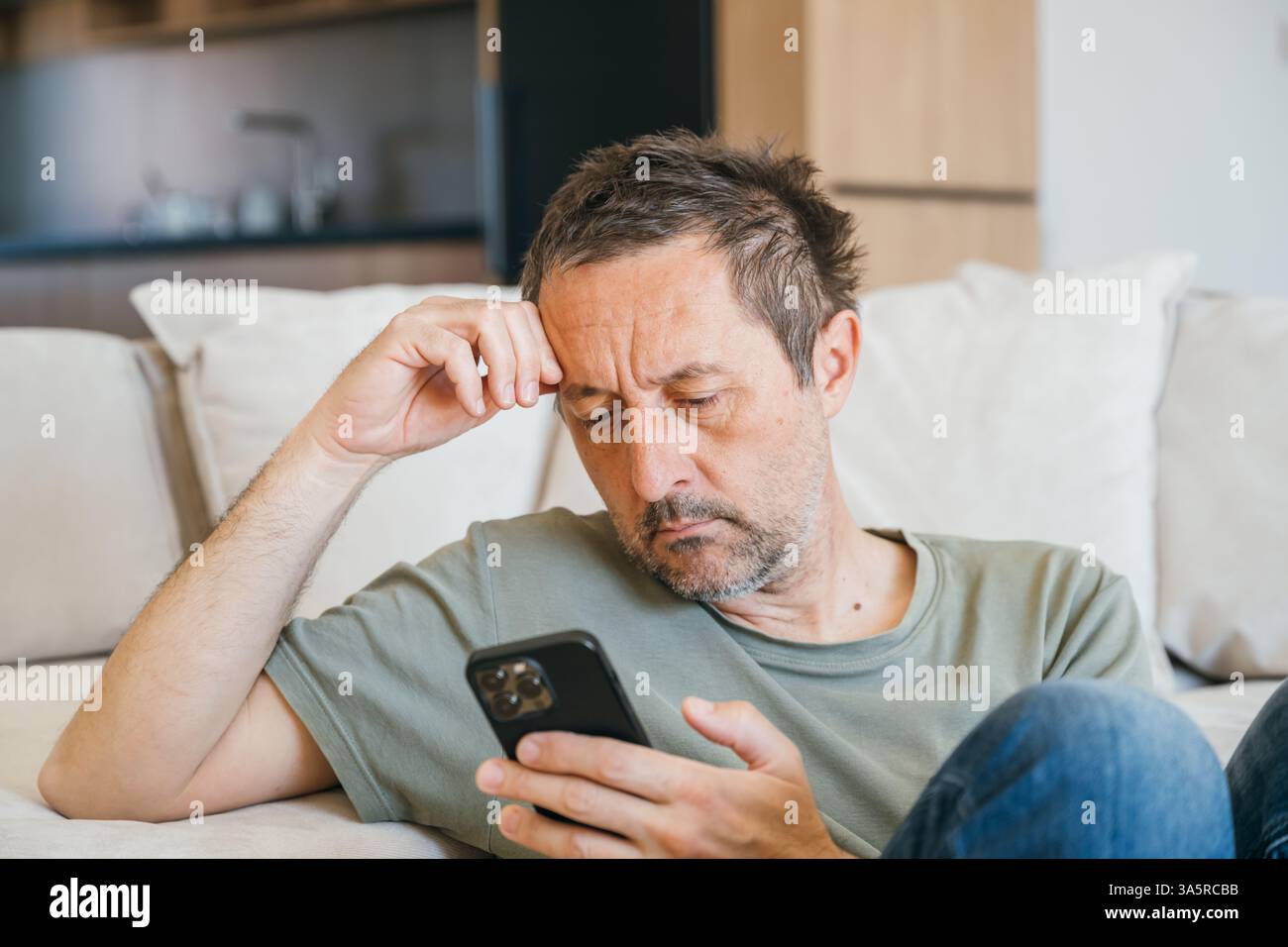 Bored man alone at home sitting on sofa in casual clothes holding ...