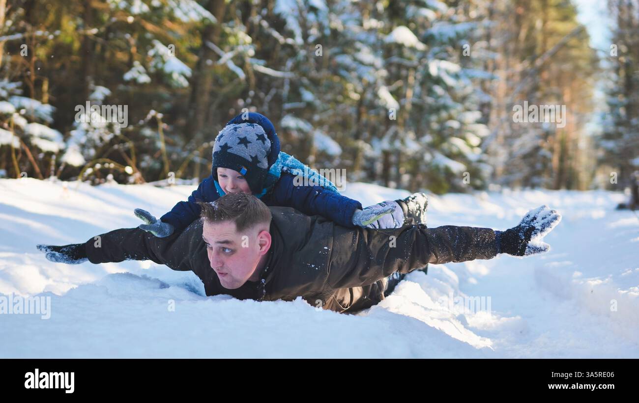 Playful father giving airplane ride to child, lying in snowy forest ...