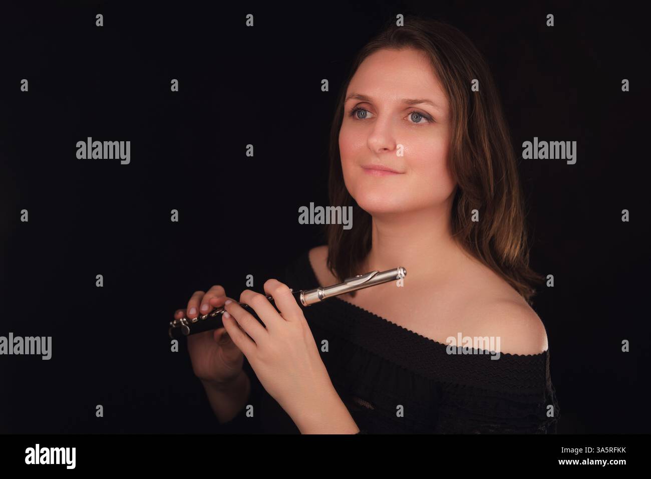 Woman holding piccolo flute against black background. Studio portrait ...