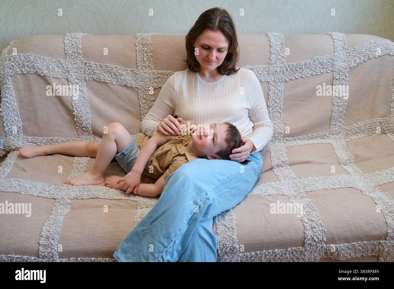 Mother and son spending time together on a cozy sofa. Loving mother caressing her child's head ...