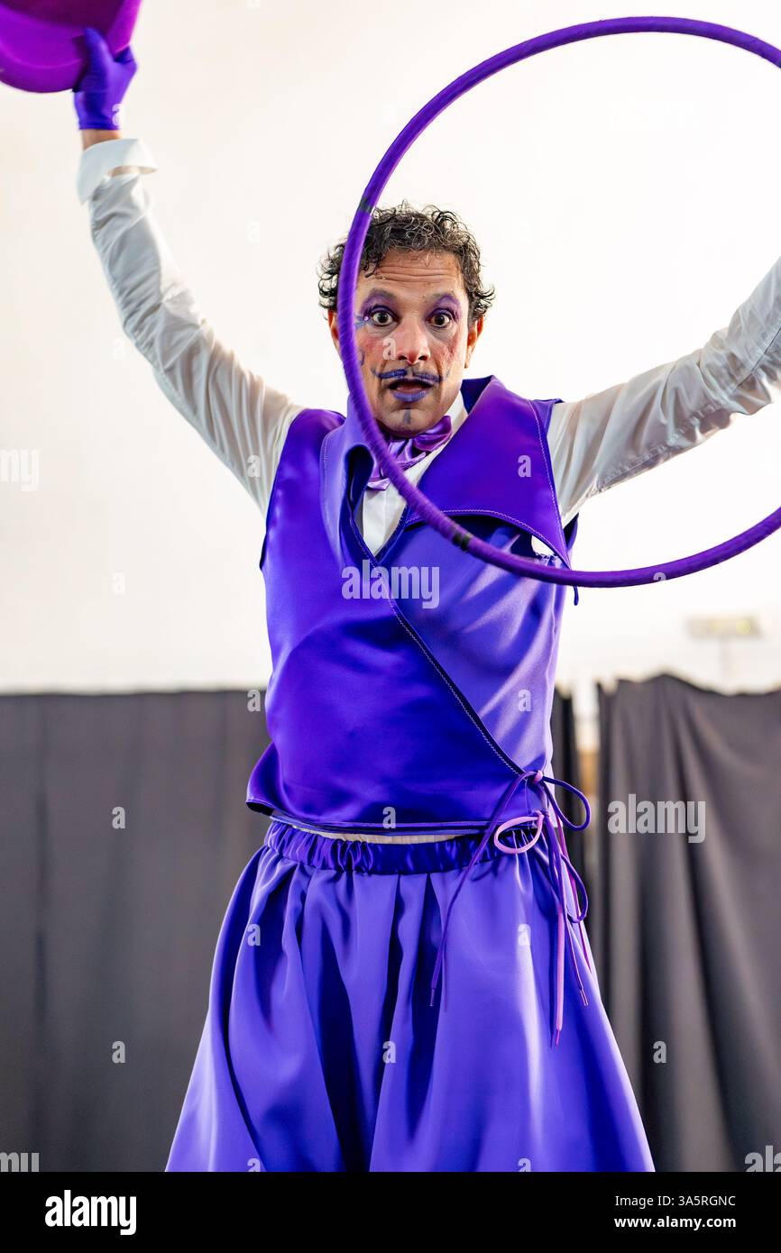 Male clown wearing purple costume and makeup juggling with purple hula ...