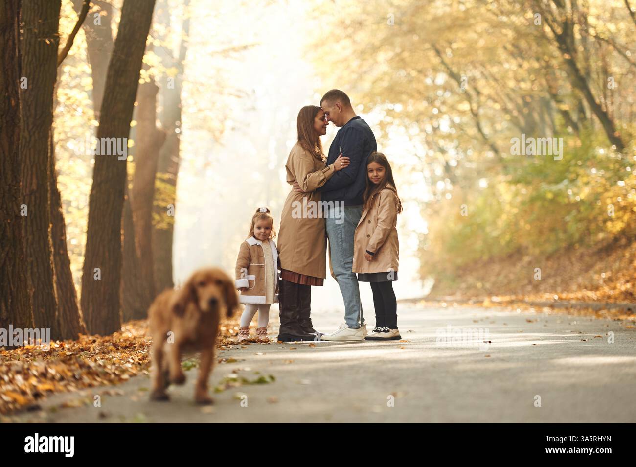 Dog is walking. Happy family of mother, father and two daughters are in the autumn park, forest ...