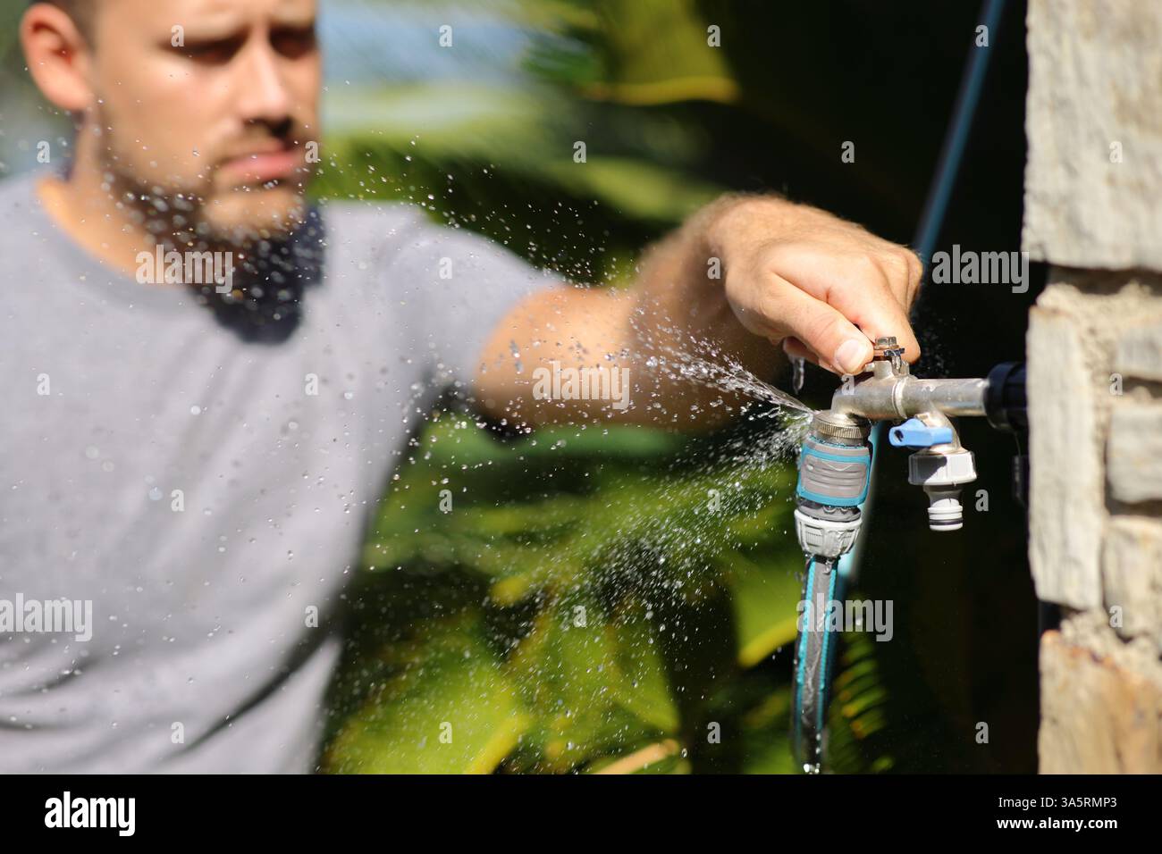 Frustrated man opening faucet with water leakage in the garden at home ...