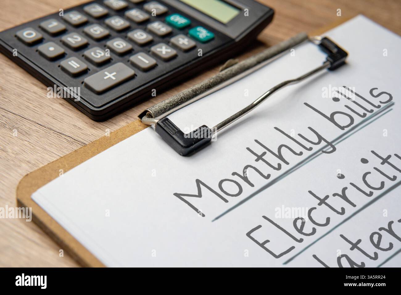 Calculator and a paper clipboard with a handwritten monthly bills list. Household budget ...