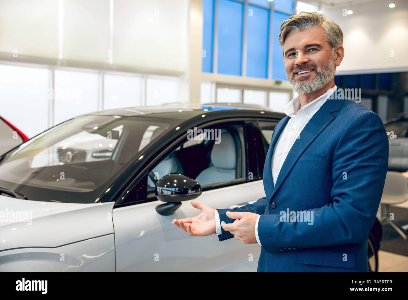 Professional salesman presenting new car in dealership showroom Stock ...