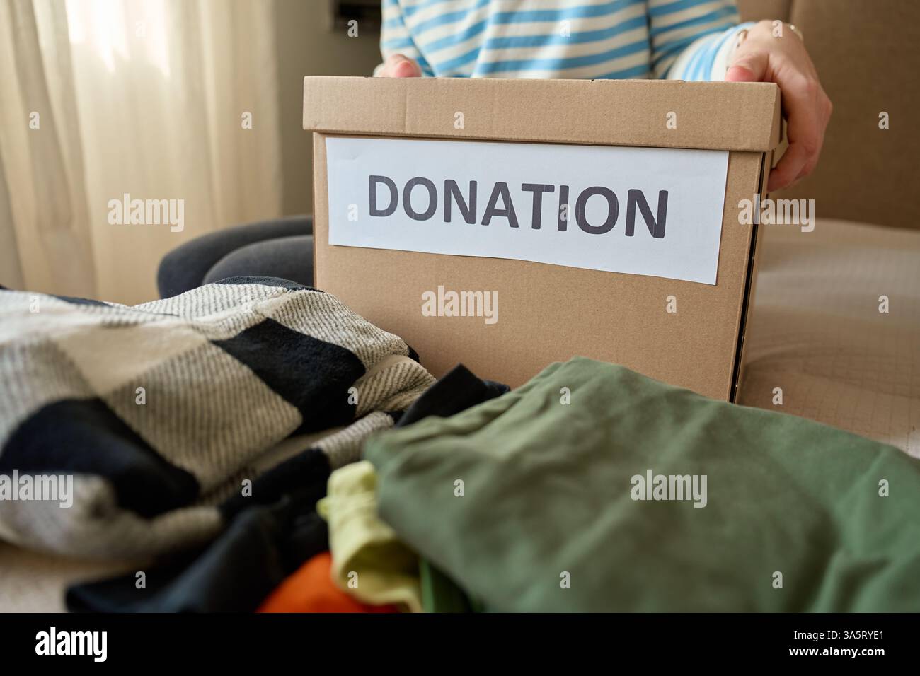 Woman holds donation box filled with clothes on bed, organizing items ...