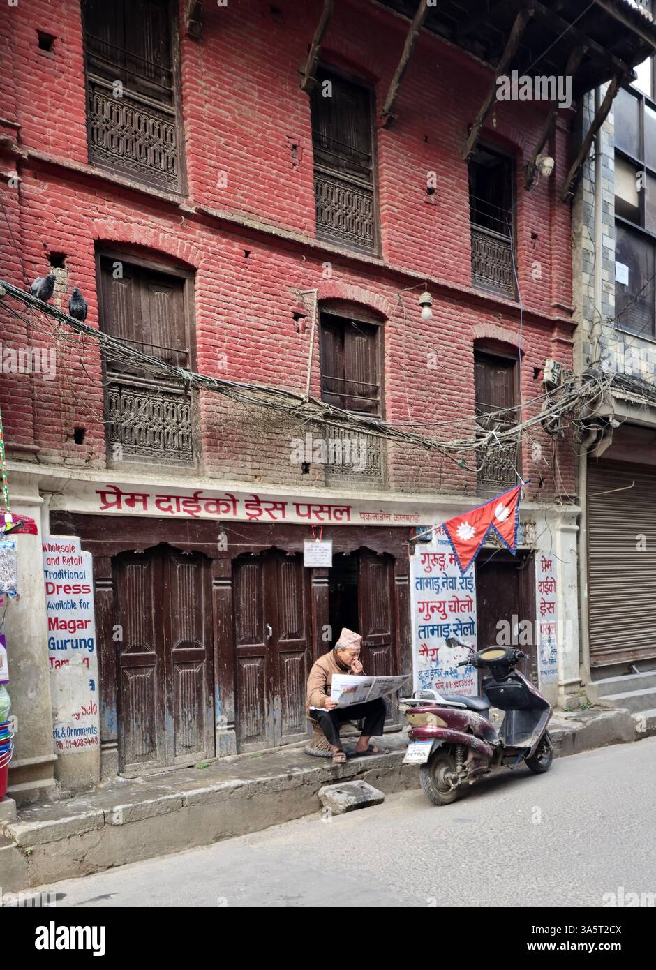 A Nepalese man reading the morning newspaper by an old house in the ...