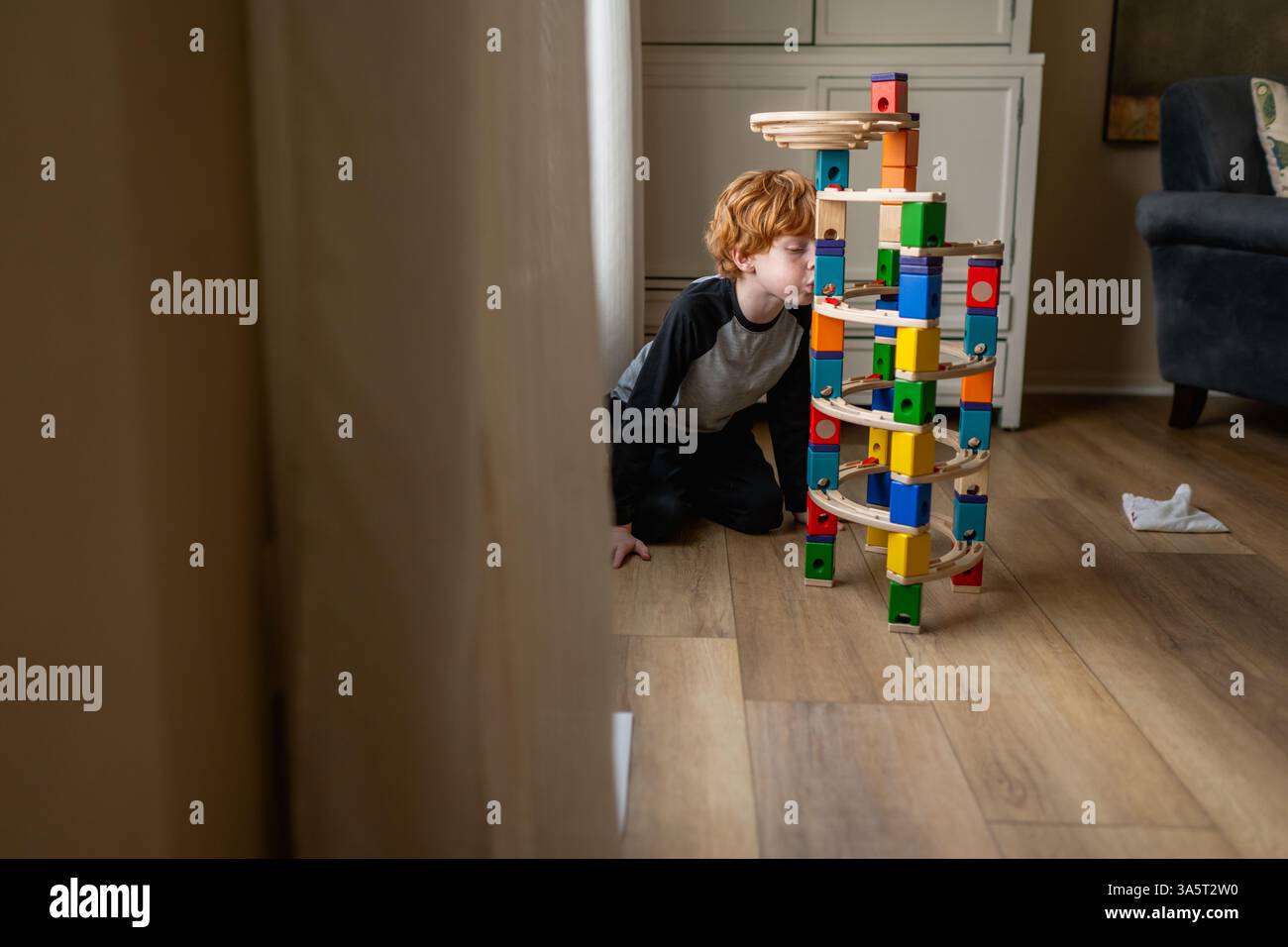 Boy blowing marbles through track of wooden block marble run at home ...