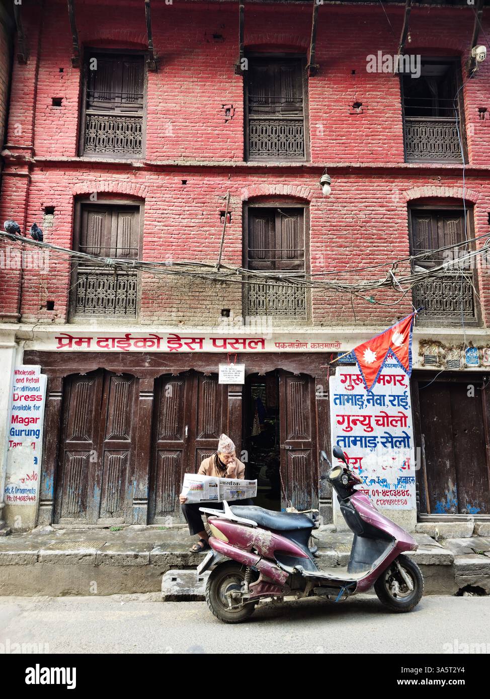 A Nepalese man reading the morning newspaper by an old house in the ...