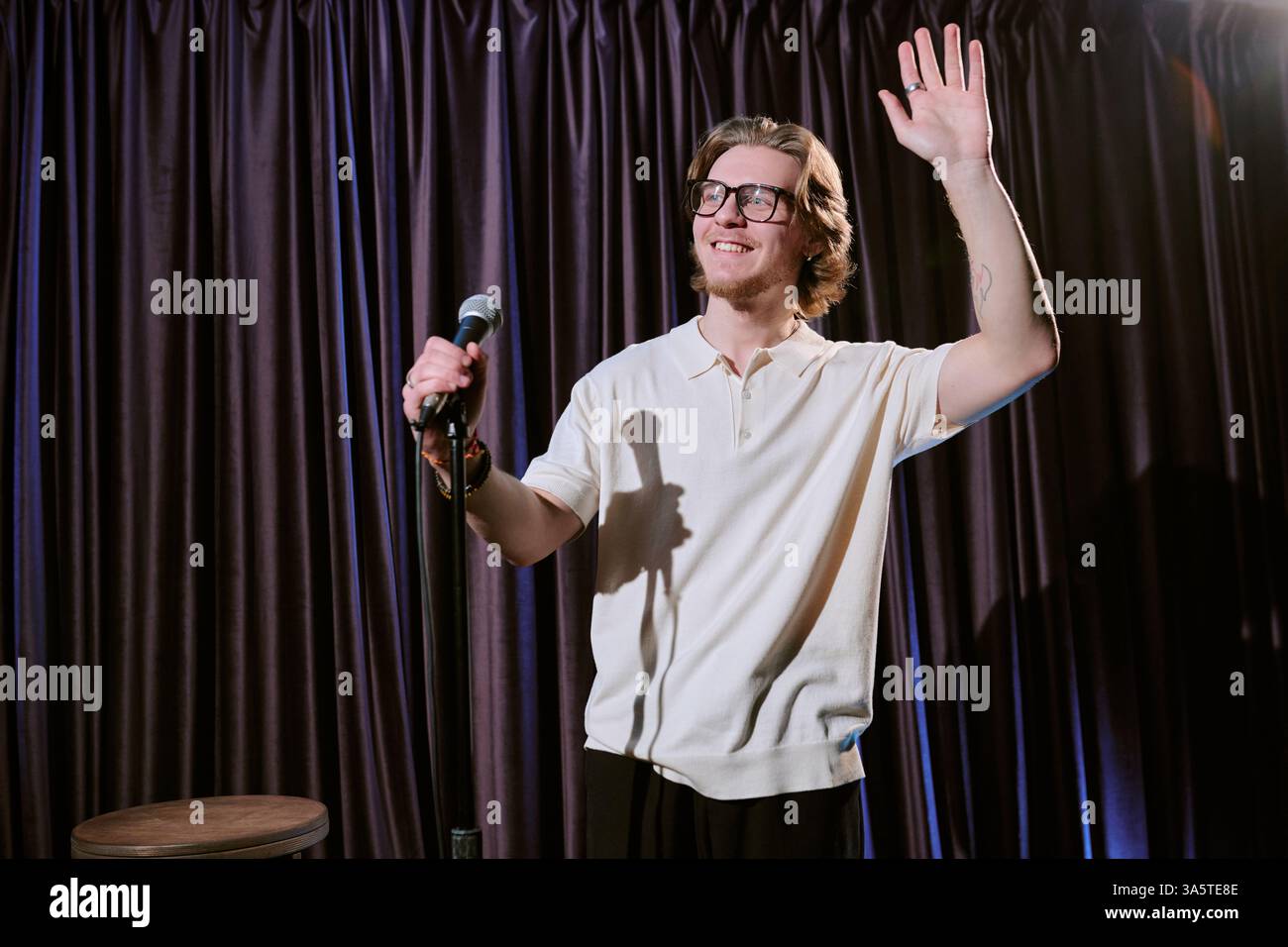 Happy male performer holding microphone with one hand raised, standing ...