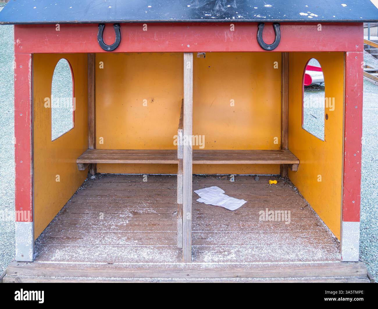 A small, colorful wooden playhouse with two open windows and a bench ...